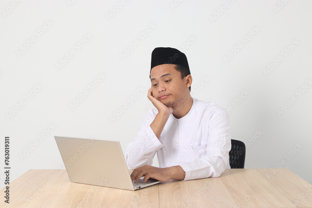Portrait of tired Asian muslim man in koko shirt with skullcap working ...