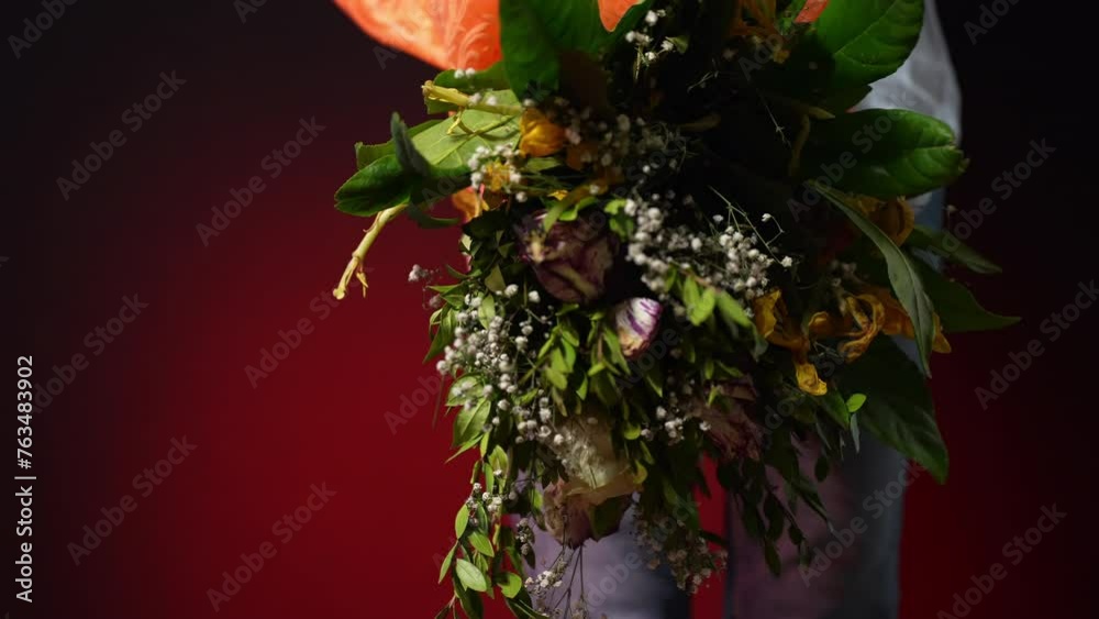 Unrecognisable woman holding faded flower bouquet against dark red ...