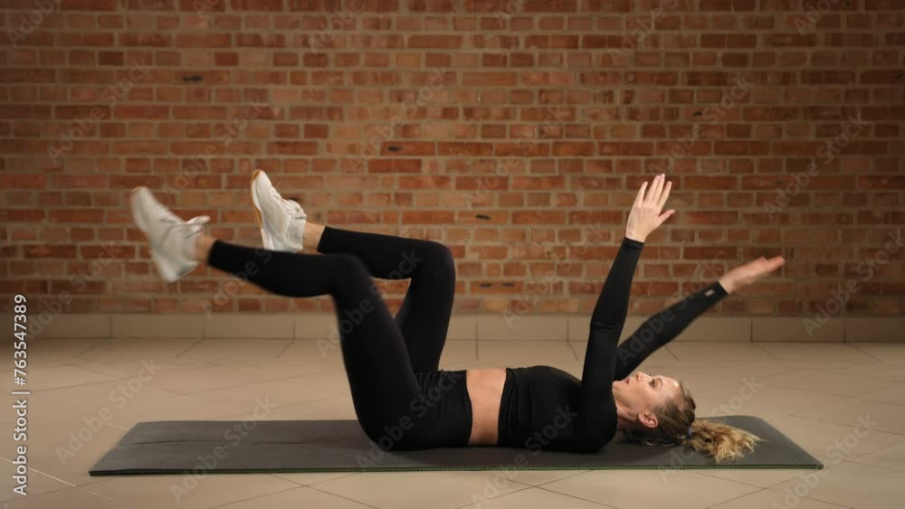 A woman on a gym mat engages her core muscles doing the left-sided dead ...