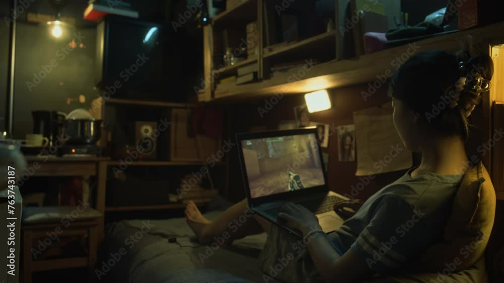 Full rear shot of young Asian woman sitting on bunk bed in dimly lit ...