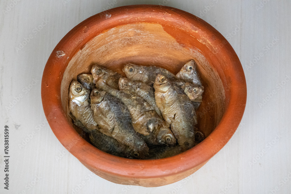 Sun-dried Puti fish (Puntius) in an earthen pot on a brown textured ...