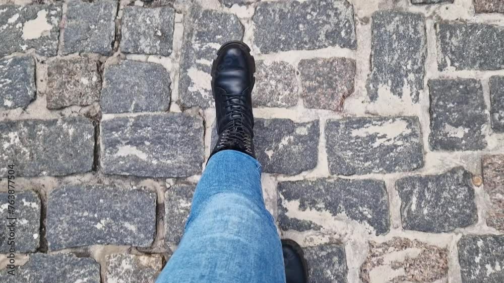 Female legs in blue jeans walk along a cobblestone path, first-person ...