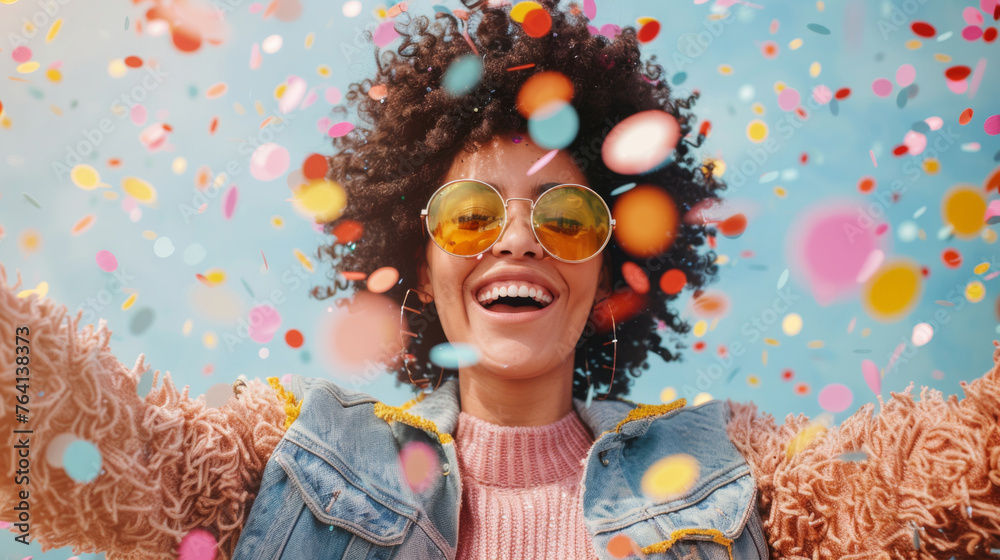 An exuberant woman raises her arms amidst a shower of colorful confetti ...