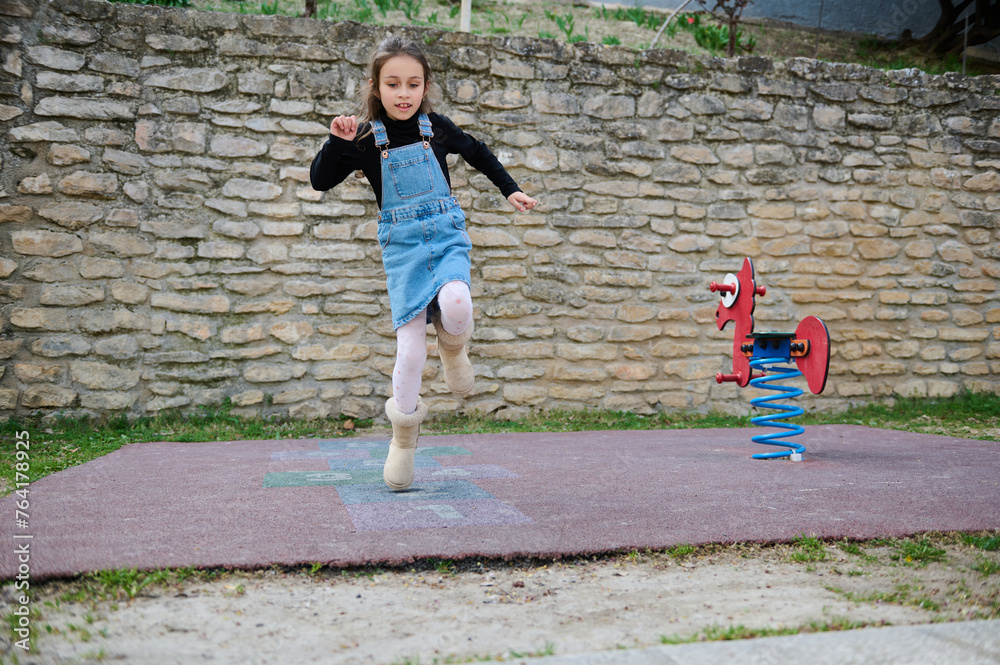 A little kid girl jumping on one leg, playing hopscotch on an urban ...