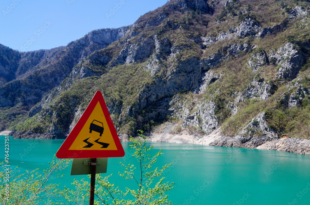 Road sign showing slippery road ahead, next to a cliff with a river ...