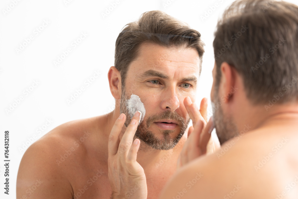 A man without a shirt is gazing at his reflection in the mirror ...