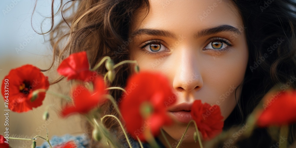 Young woman in a vintage dress holding a red poppy flower up to her ...
