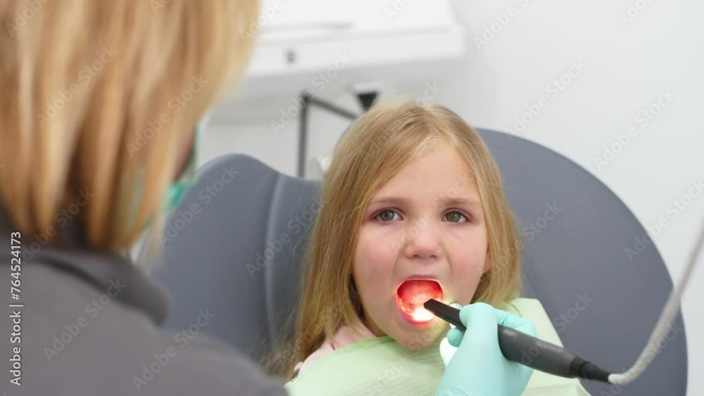 Little girl sits in dental chair. Female dentist examining child's ...