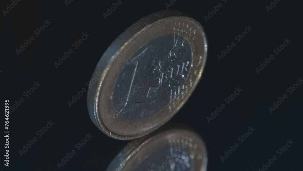 A 1 euro coin rotated on a mirror surface in the dark, the light is ...