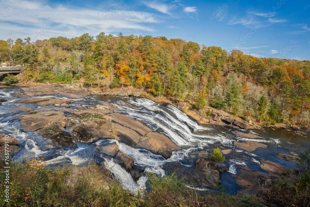 In a backdrop of fall foliage and blue sky, the scenic Towaliga River cascades downstream over ...