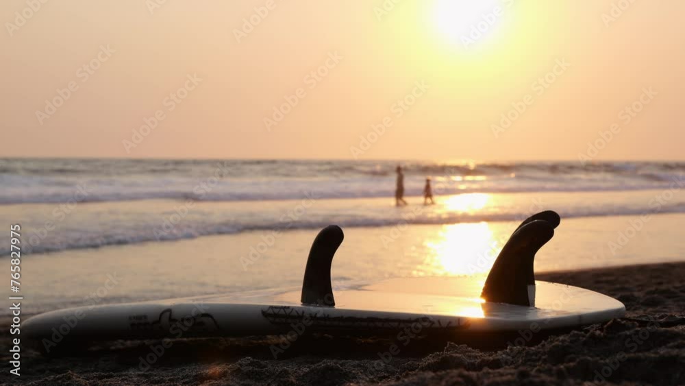 Close-up surfboard lying on sand along ocean shore, illuminated by ...