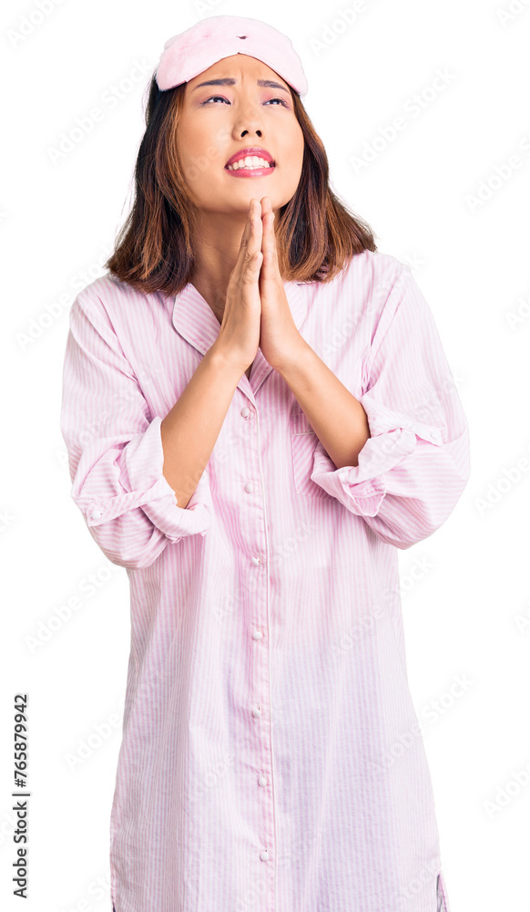 Young beautiful chinese girl wearing sleep mask and pajama begging and ...