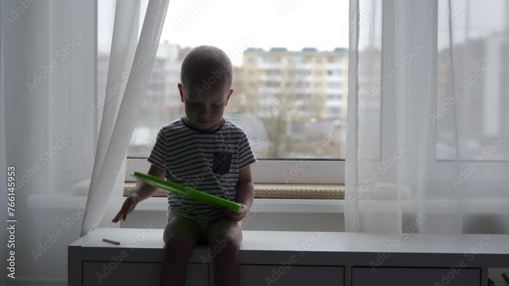 3-year-old child at the window drawing with pen on electronic drawing ...