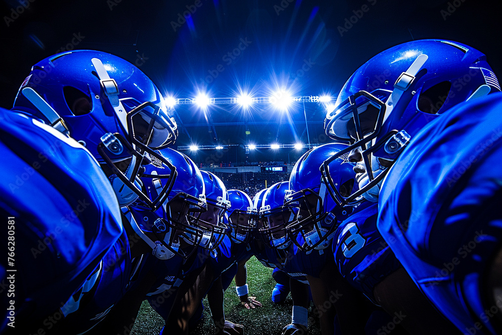 College football players in a huddle, lit by stadium lights ...