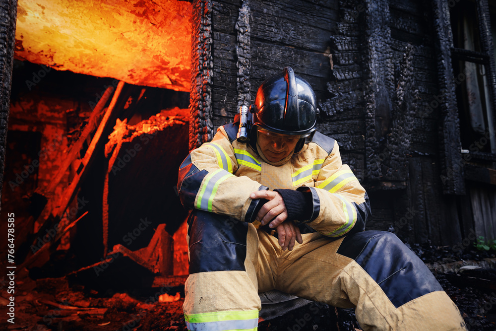 Sad fireman sits next to burning house, hard profession of rescue ...
