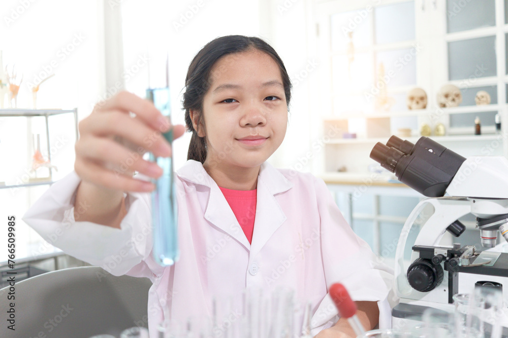 Cute young scientist schoolgirl in lab coat show blue chemical test ...