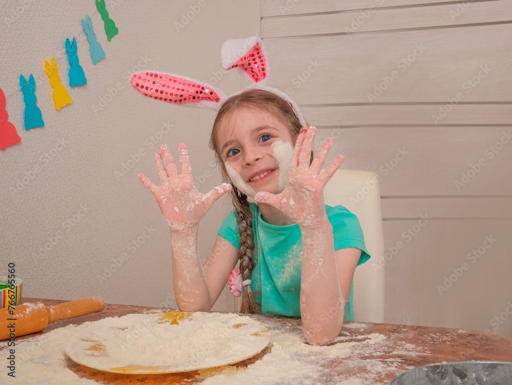 A little girl in rabbit ears at the table shows her hands stained with ...