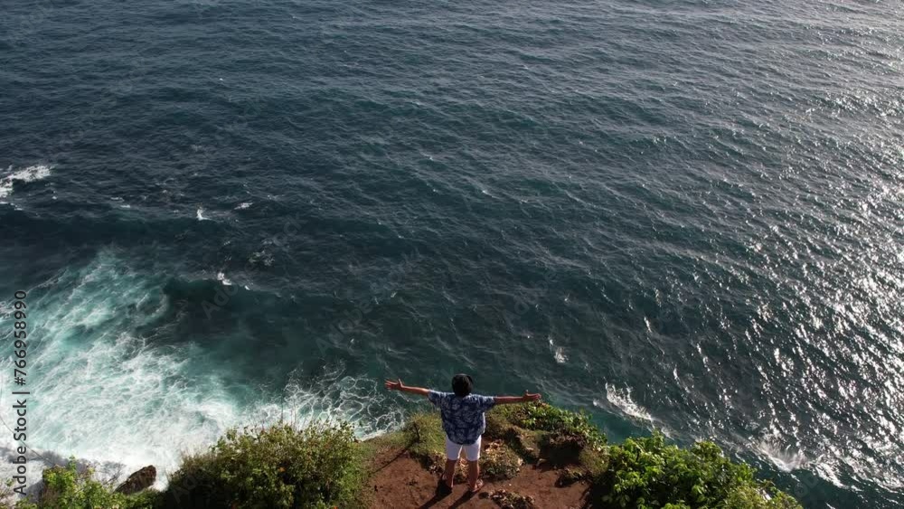 Man stand on edge of cliff, spread arms wide and looking into the ...