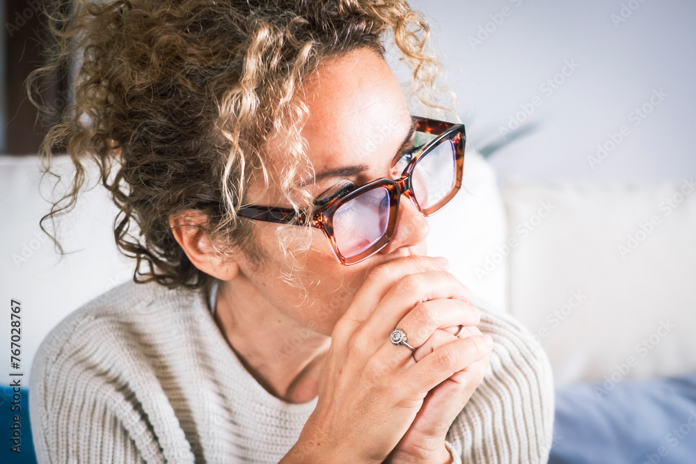 Worried adult woman sitting on sofa at home clasped hands and thinking ...