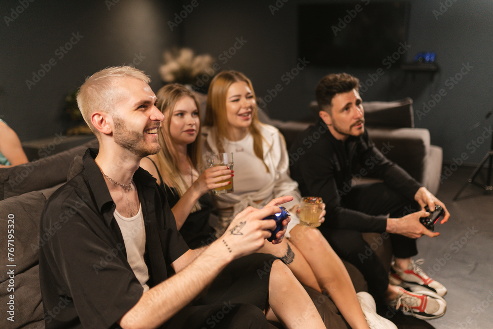 Women sit between men playing console in game room. Best friends form ...