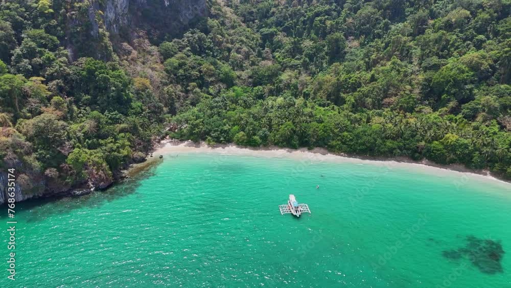 Drone footage of a filipino boat in a turquoise lagoon near a steep ...