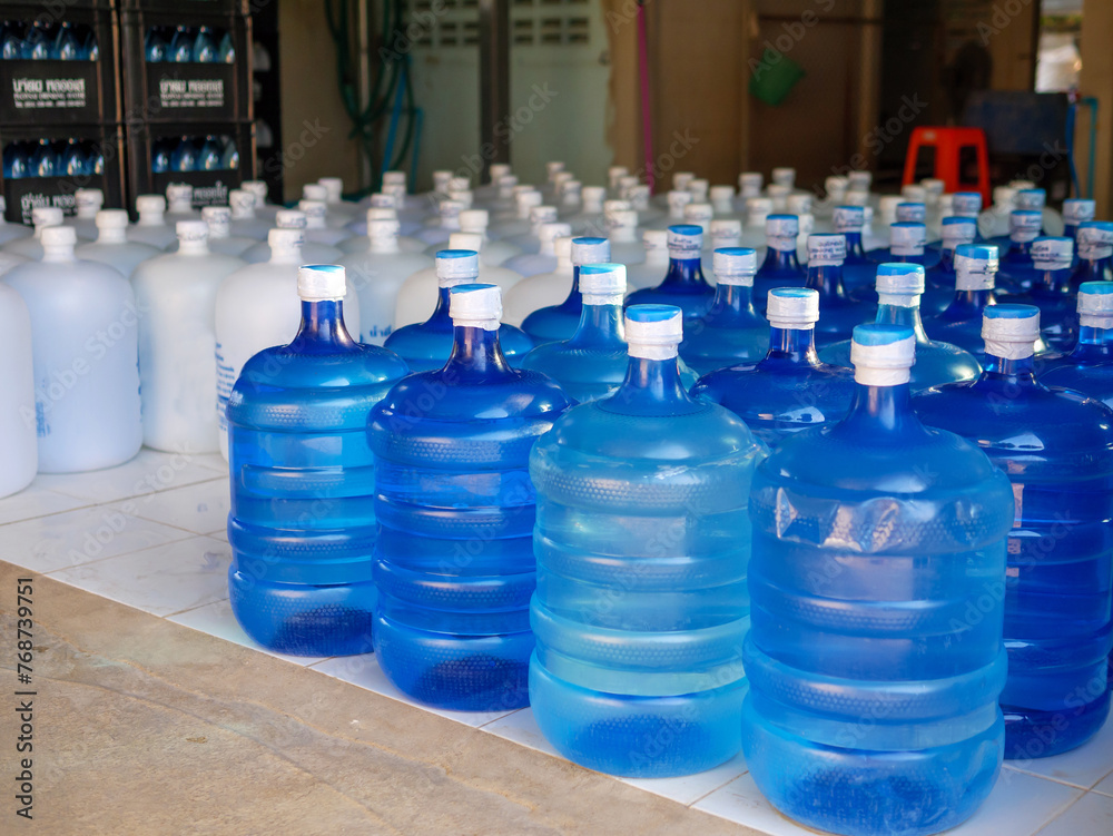 Many blue gallons and white gallon of drinking water are lined up in a ...