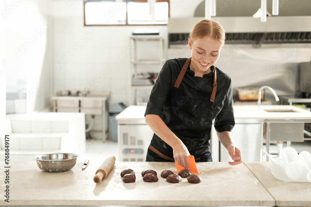 Medium shot of a young female pastry chef shaping small pieces of ...