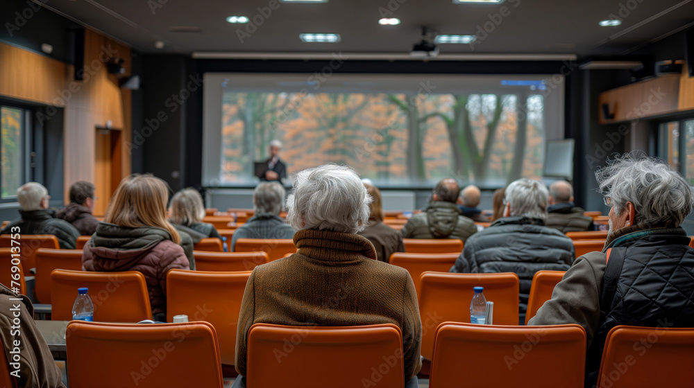 A group of attentive senior citizens sit in a lecture hall, focusing on ...