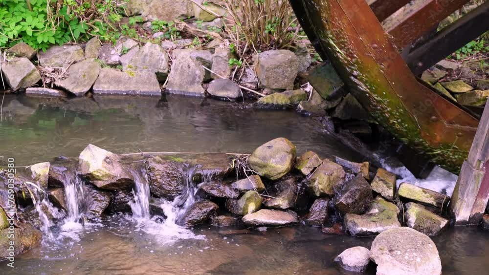 Water streaming through time-honored waterwheel, its wood rich with ...