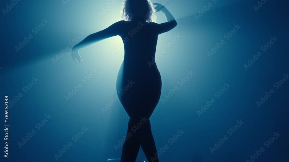 A captivating silhouette of a woman performing a sensual solo dance in dim, moody blue light ...