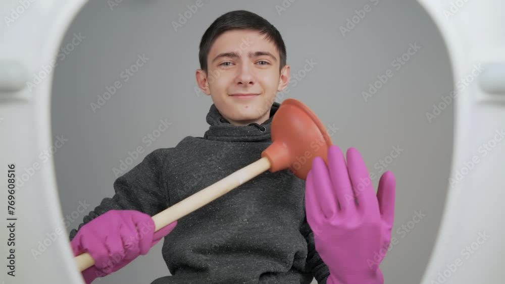 Boy teenager scrubbing and cleaning toilet in restroom using plunger ...