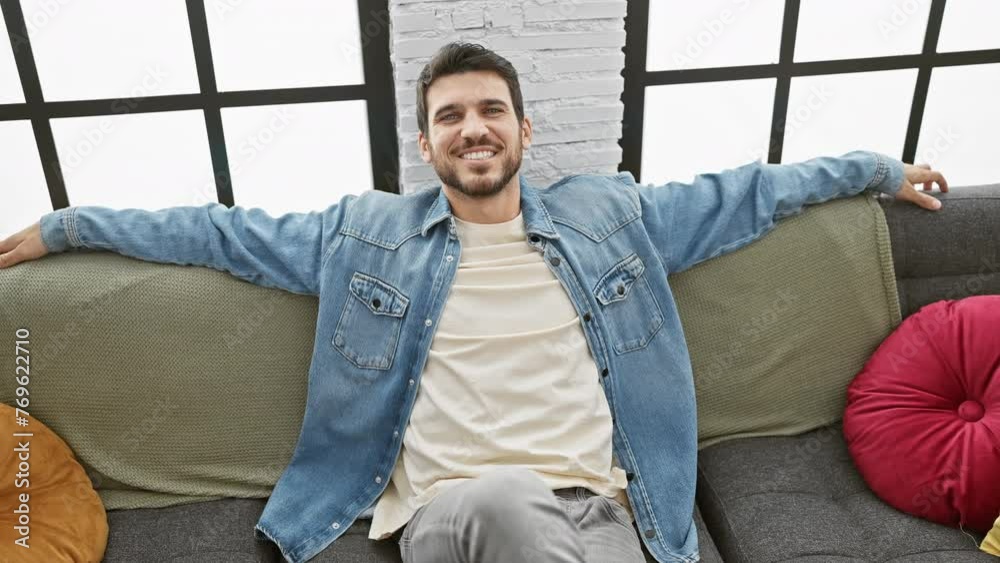 Handsome young hispanic man with a beard wearing a denim jacket sits ...