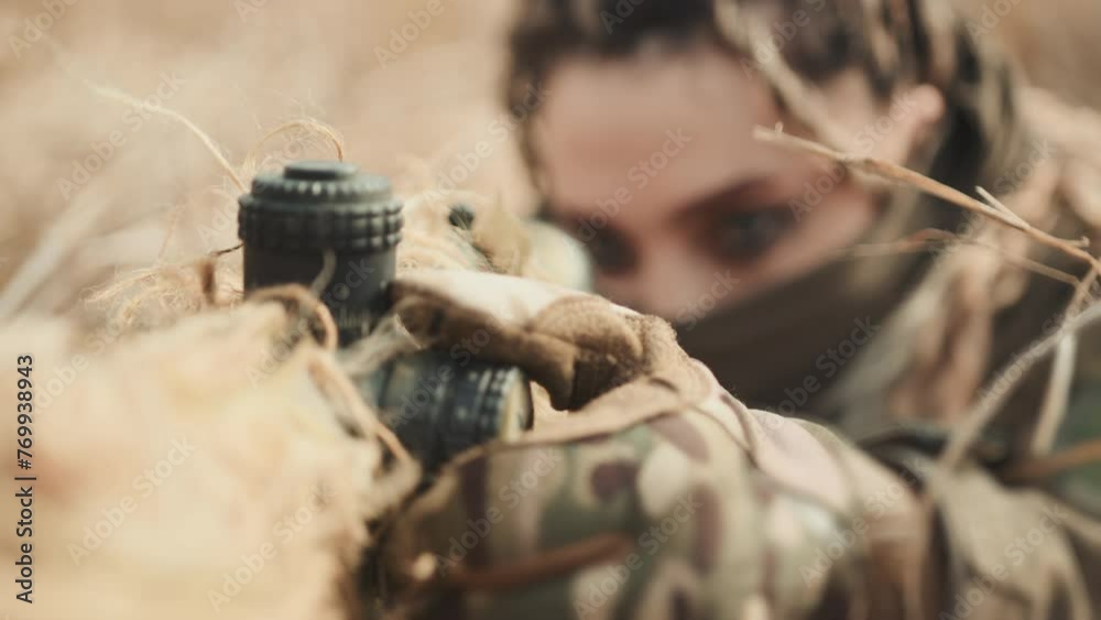 A sniper woman carefully adjusts the optical scope on her sniper rifle ...