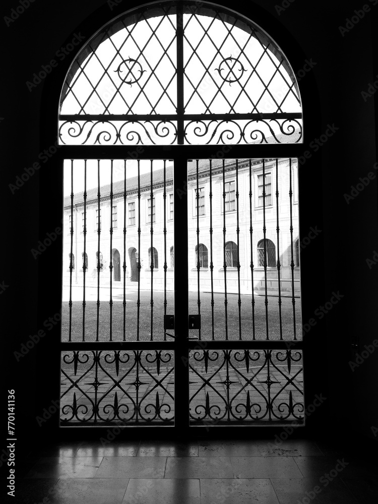 Black and white image of an ornate iron gate with a view of a courtyard ...