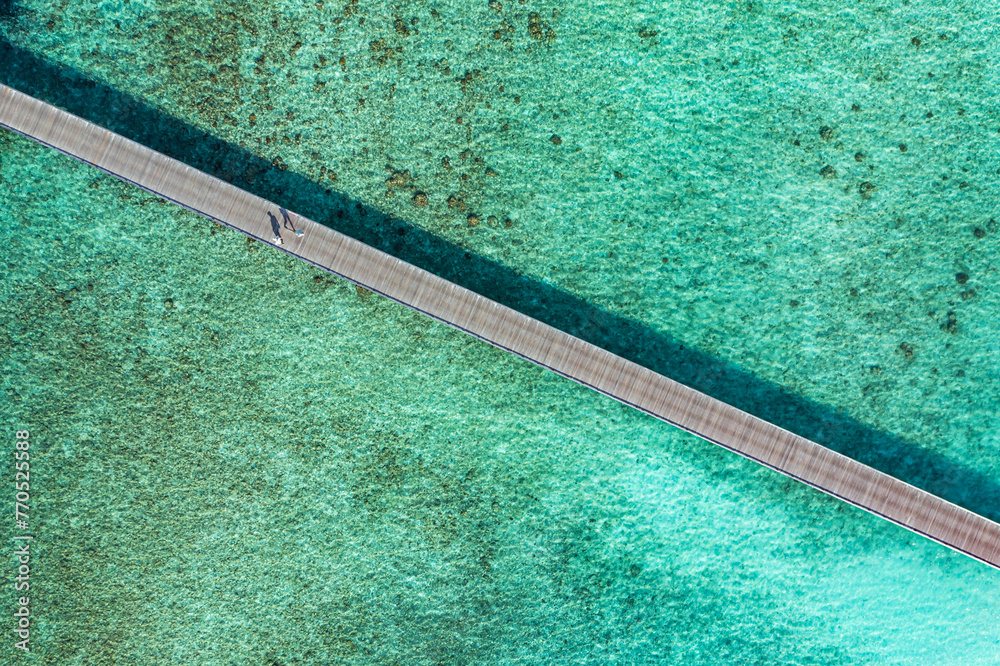 Birds eye view of wooden jetty leading out over pristine crystal clear ...