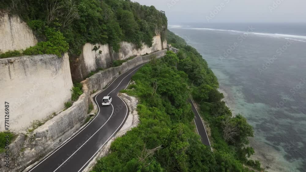 Aerial view, a white car driving along the cliff-side asphalt road and ...