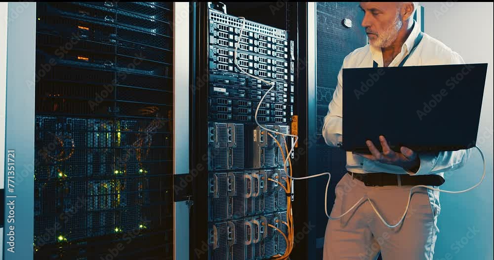 Mature man in server room with laptop, inspection on network and ...
