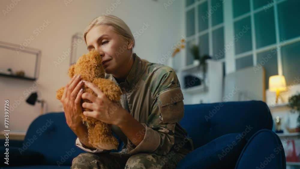 Sad female army officer hugging a teddy bear toy, missing her family ...