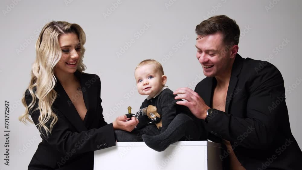 Positive Caucasian parents with their little kid sitting on the cube ...