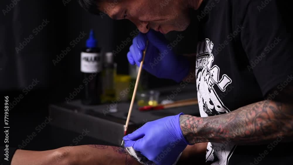 Male tattoo artist performs traditional Thai bamboo tattoo on Asian ...