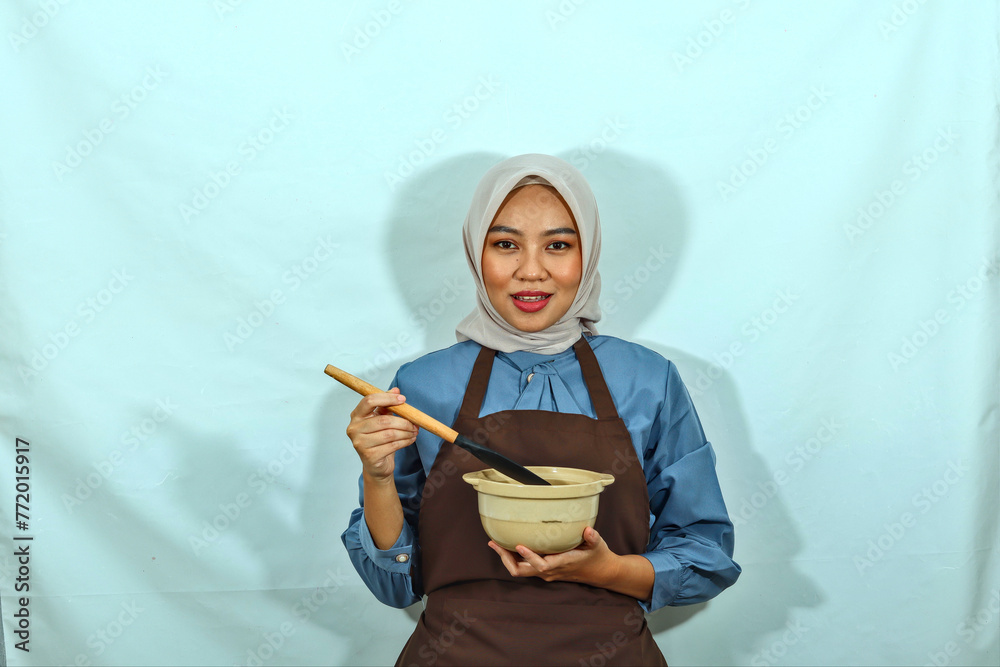 beautiful Asian woman in a brown apron and hijab holding a spoon and ...