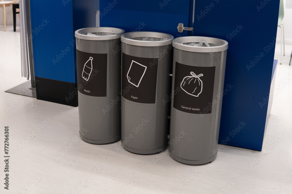 A row of three recycling bins lined up next to each other indoors. The ...