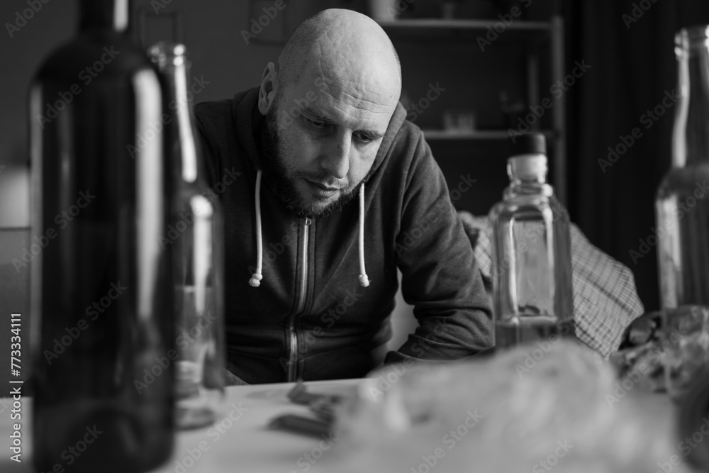 black and white portrait of alcoholic depressed man sitting near table ...