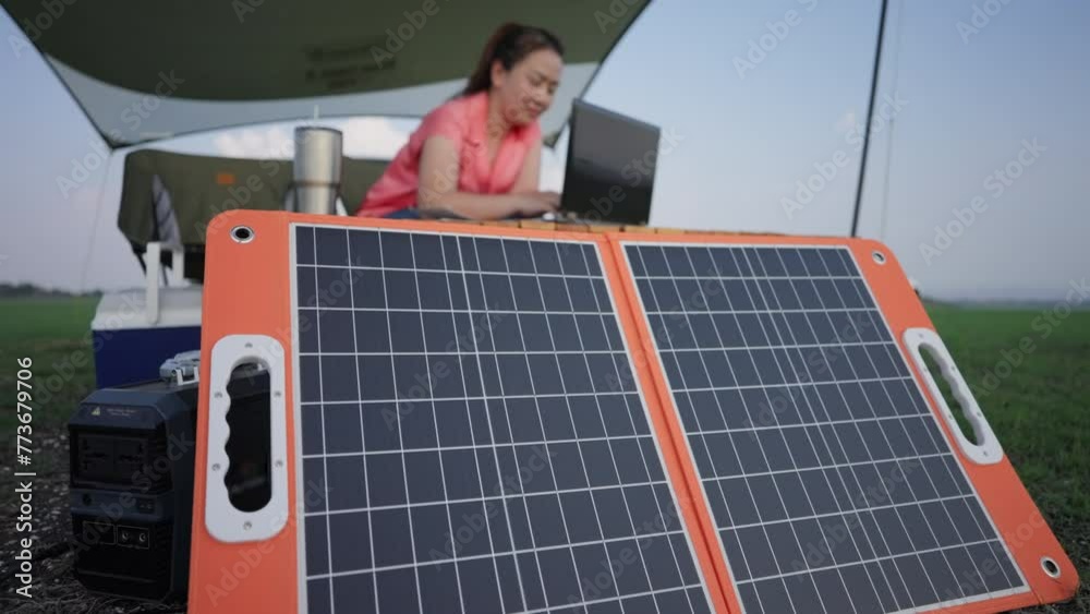Asian woman working on laptop powered by a portable solar panel or ...
