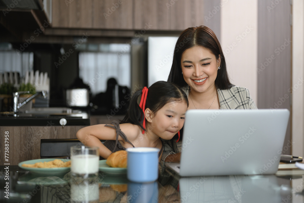 Beautiful single mother working on laptop at home with daughter ...
