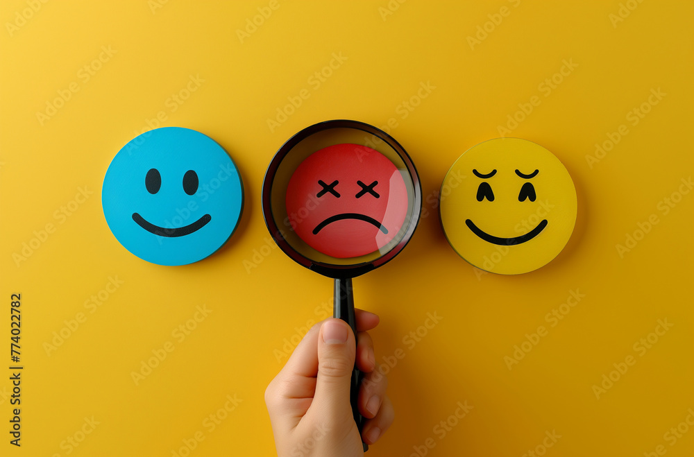 A hand holding a magnifying glass over blue and red smiley face icons ...
