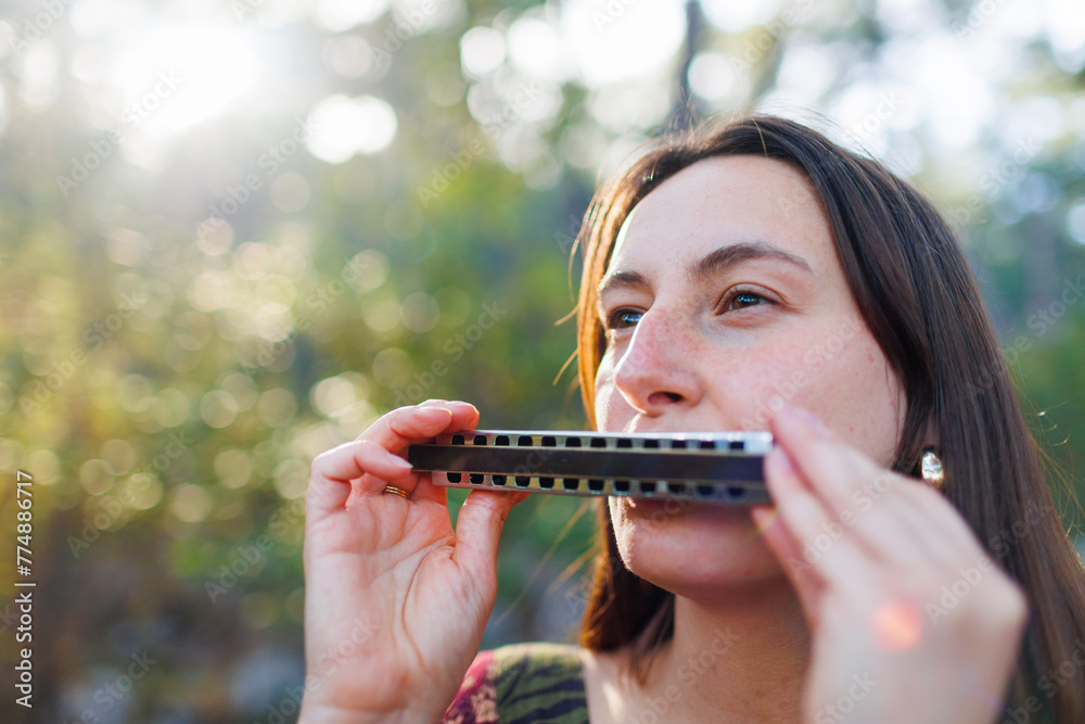 young girl plays the harmonica in the forest. the girl loves to play ...