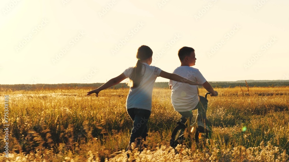 happy girl runs catching up with boy, child boy rides bicycle, son ...
