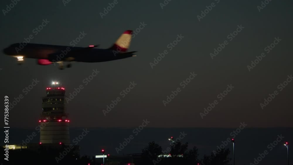 An airliner with illuminated landing lights flies low at night over a ...