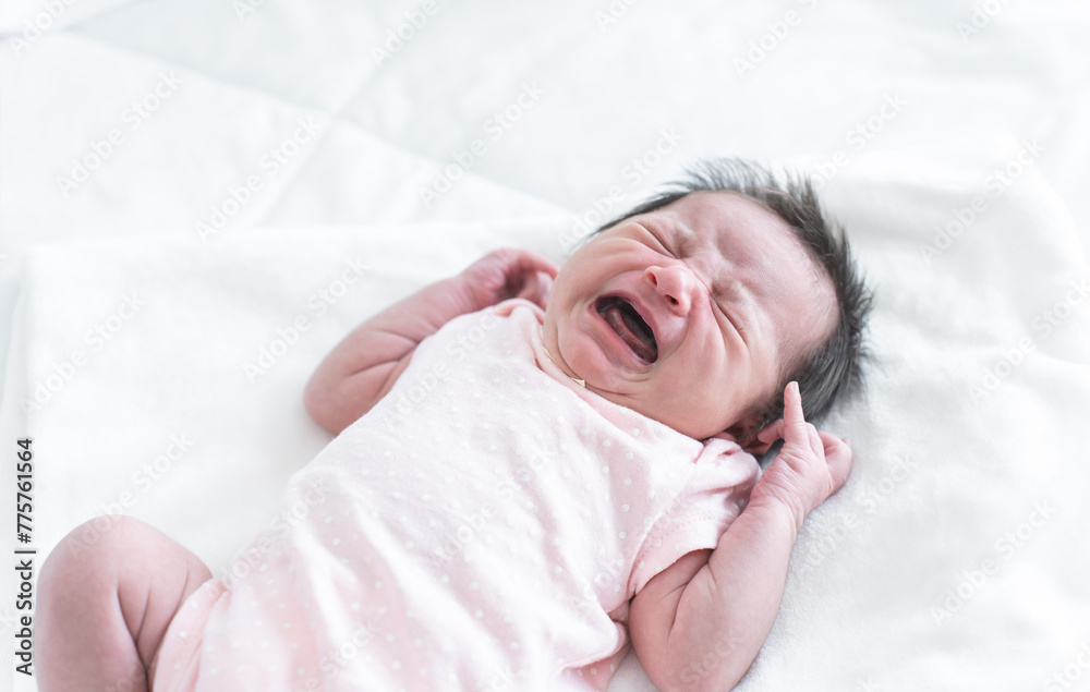 Newborn baby girl crying and screaming, lying on bed at home. Asian ...